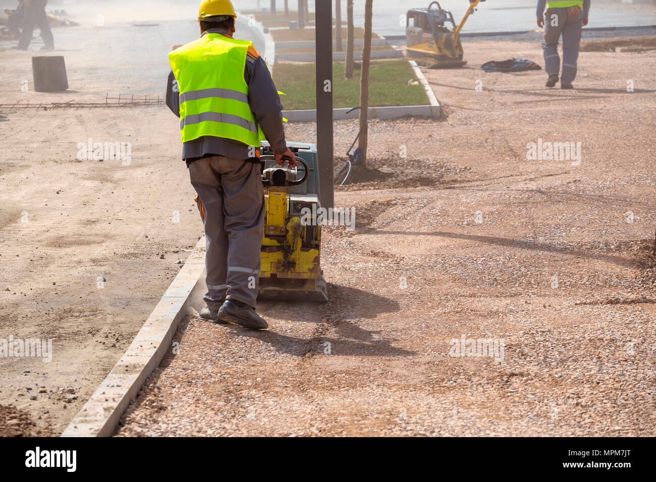 City park reconstruction with worker compacting soil using compactor ...