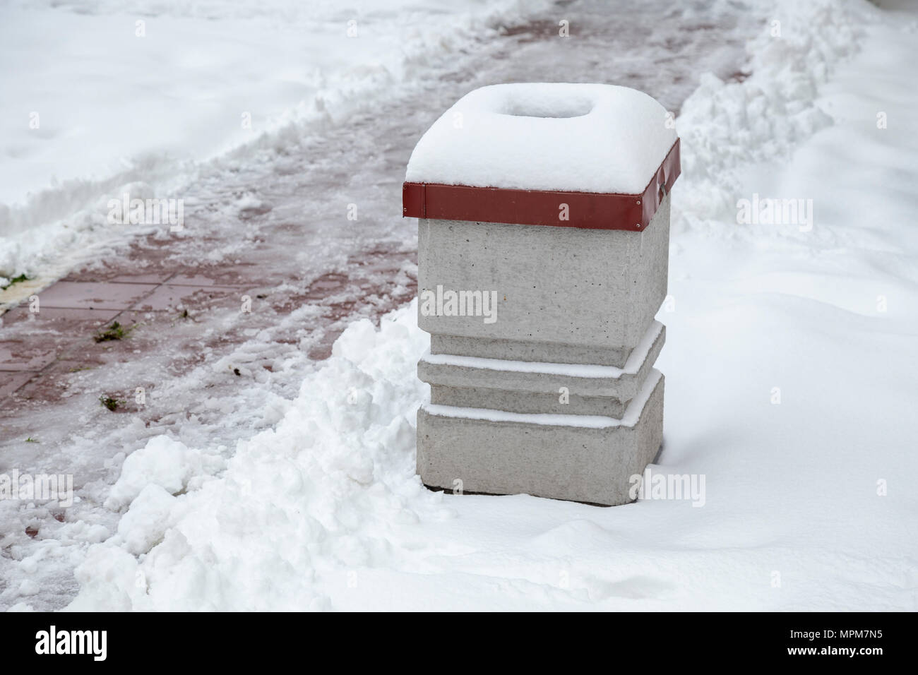 Concrete garbage can covered in snow on street. Outdoor at winter time ...