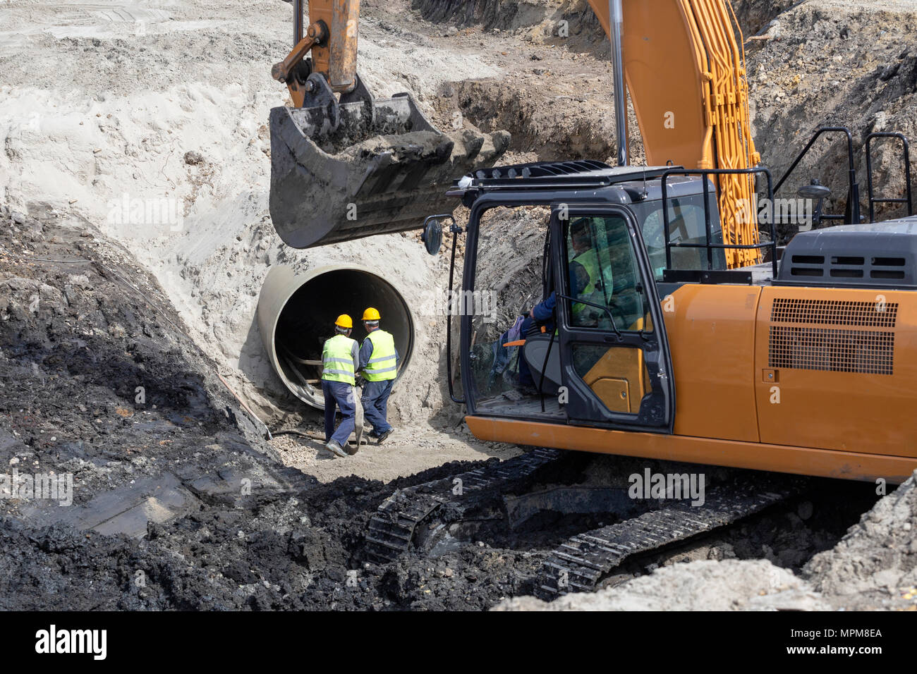 Excavator and workers making trench bed for new pipeline construction ...