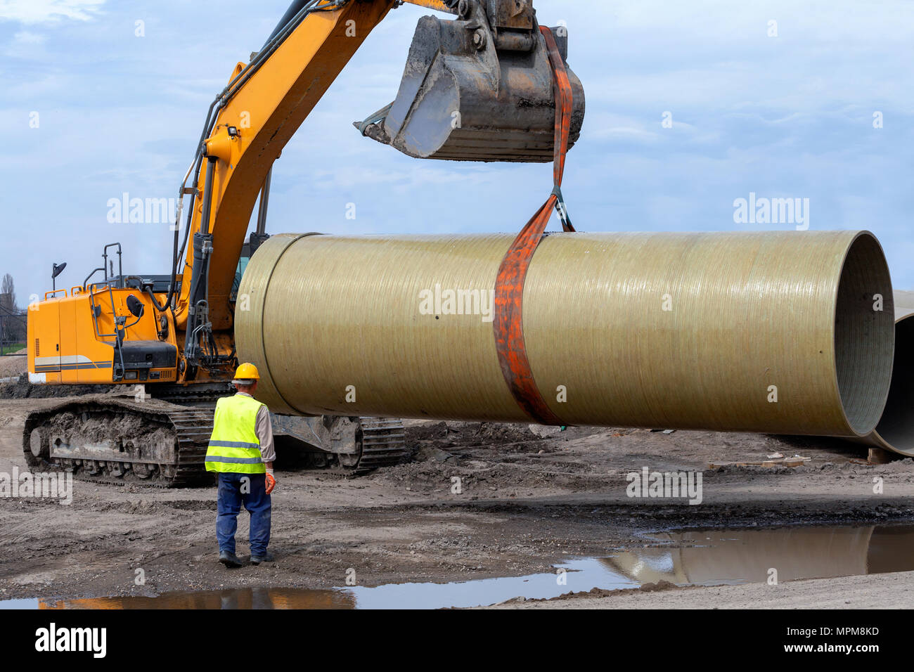 Excavator bucket lifting large underground pipe with worker helping to ...