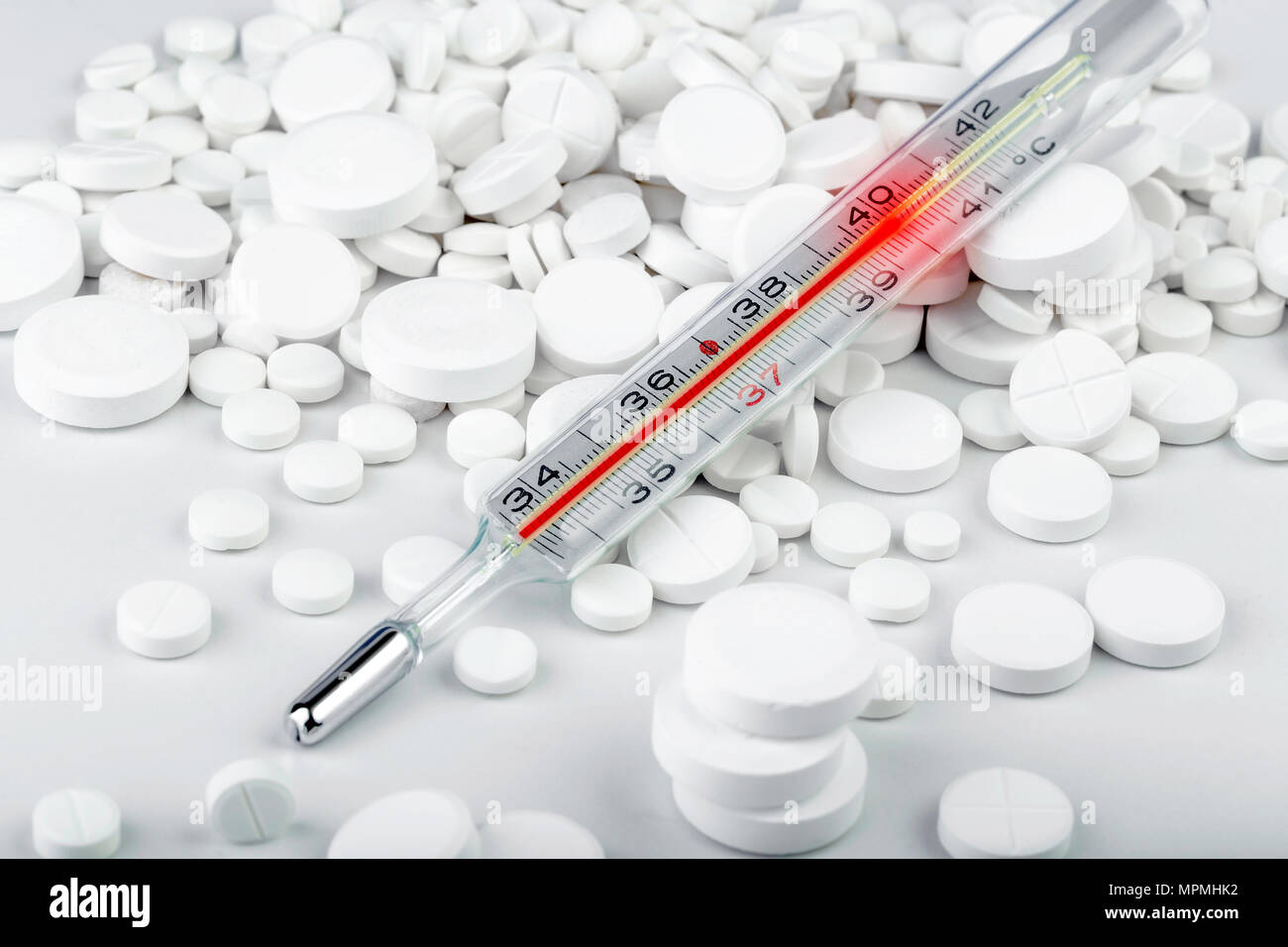 Disease and fever. Bunch of white tablets with thermometer. Scattered ...