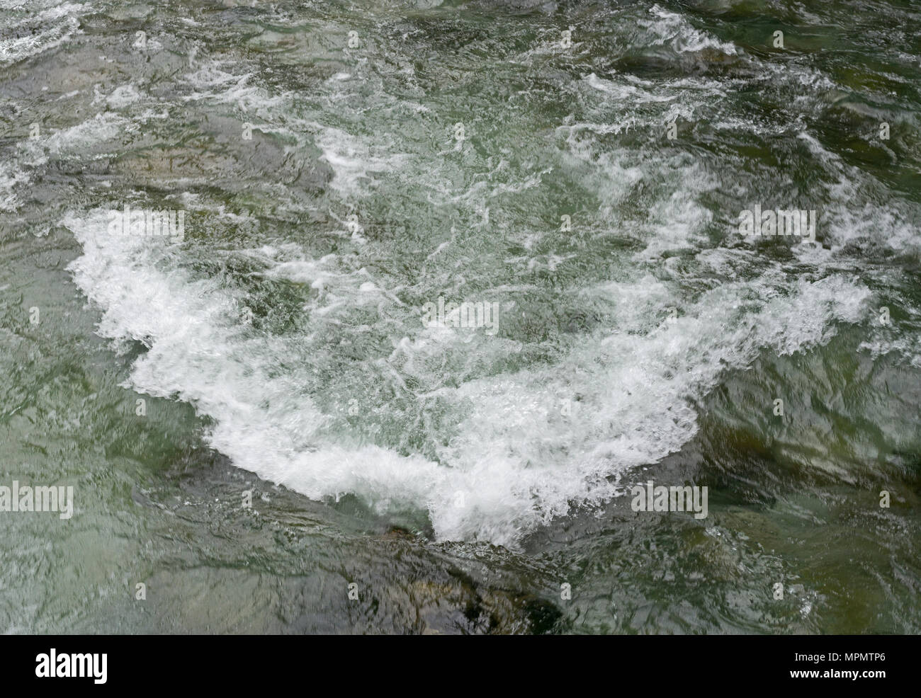 Water in river from mountain lake flowing over rocks in river causing ...