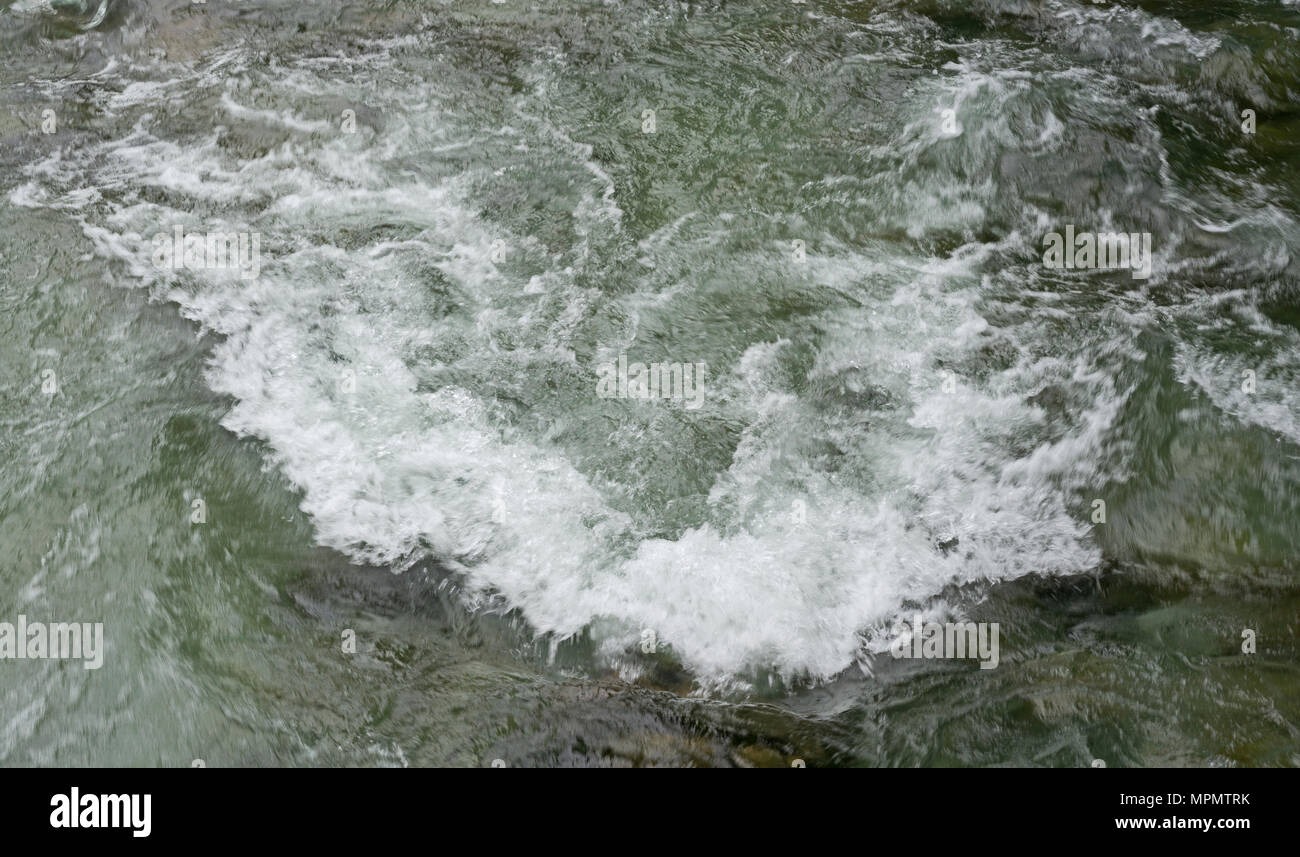 Water in river from mountain lake flowing over rocks in river causing ...
