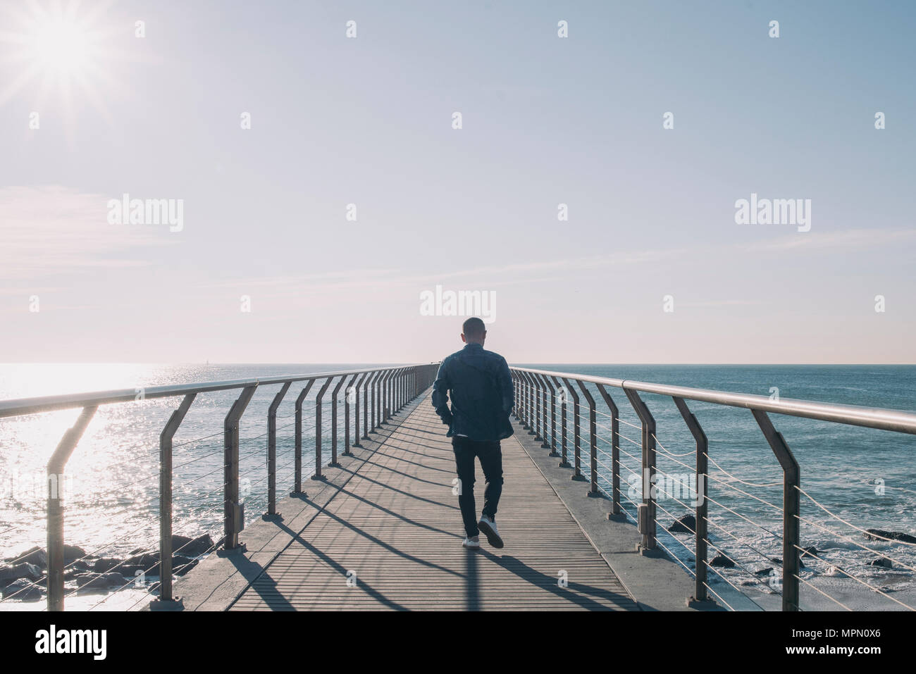 Back view of man walking on boardwalk at backlight Stock Photo - Alamy