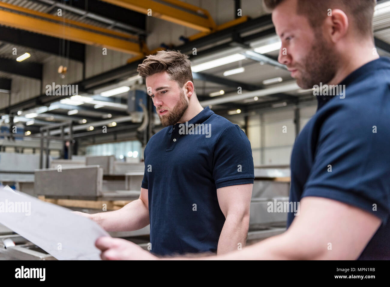 Two men looking at plan in factory Stock Photo - Alamy