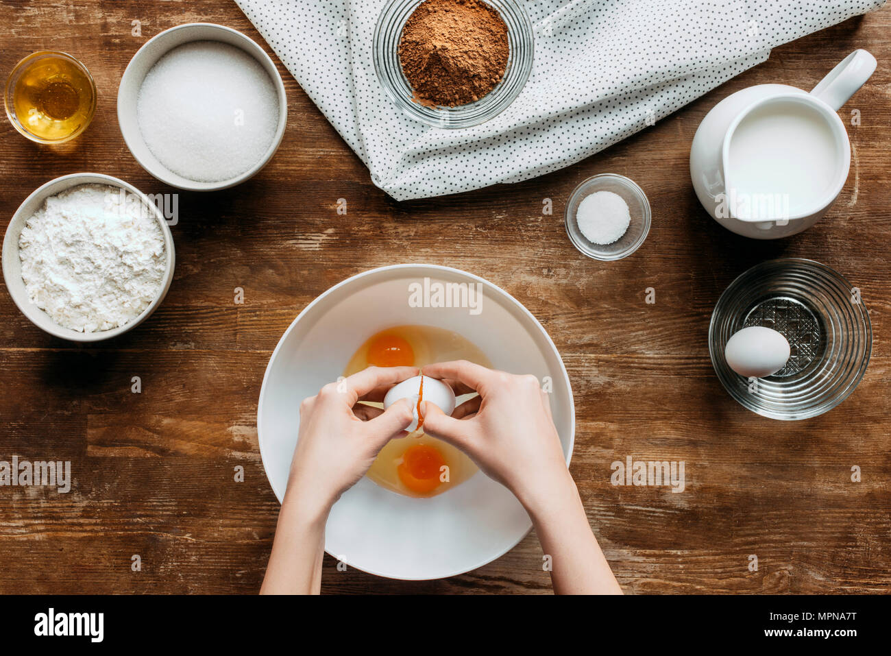 cropped shot of woman breaking eggs into bowl for pastry on wooden ...