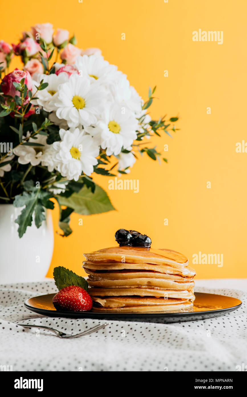 delicious stacked pancakes with berries and syrup on table with flowers ...