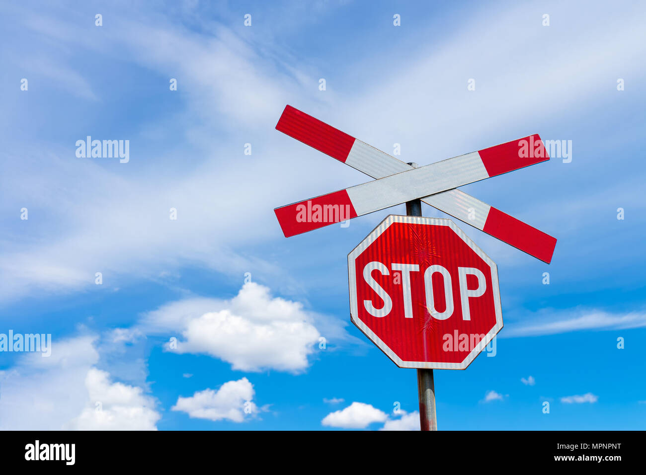 Red stop sign with railway cross sign and blue sky with white clouds in ...