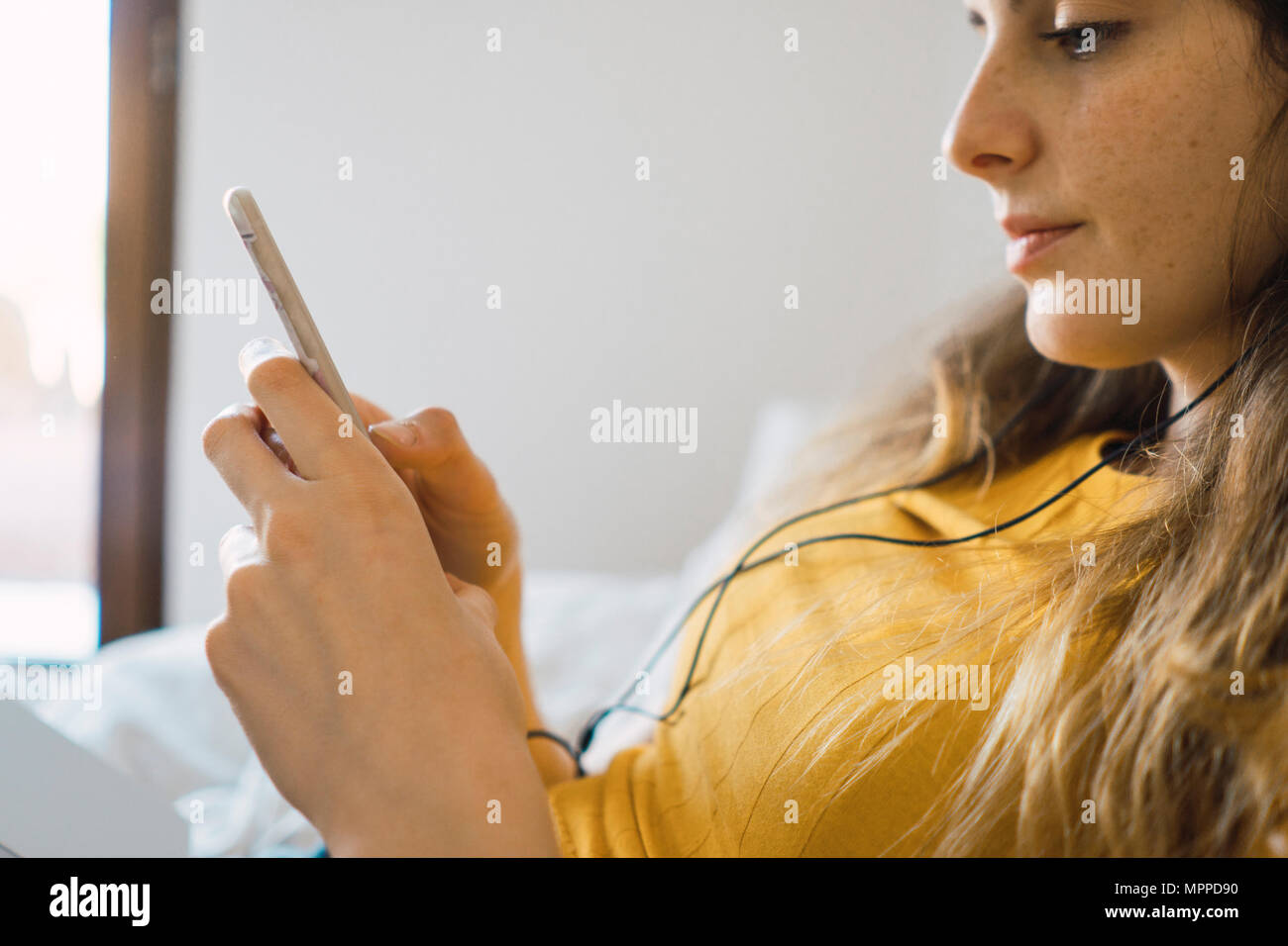 Young woman lying on bed using cell phone and headphones Stock Photo ...