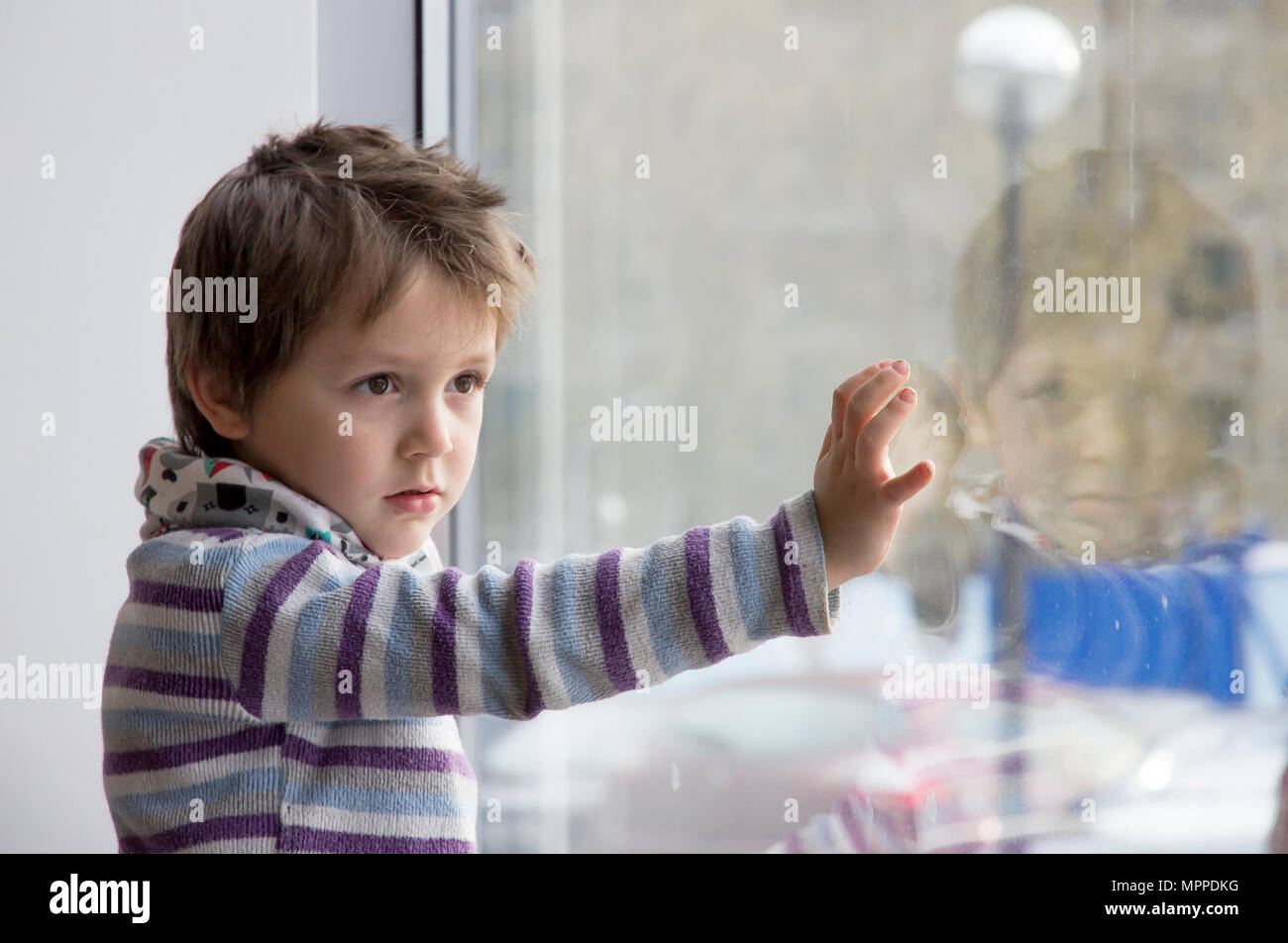 Pensive little boy of five years standing at window cafes and is ...