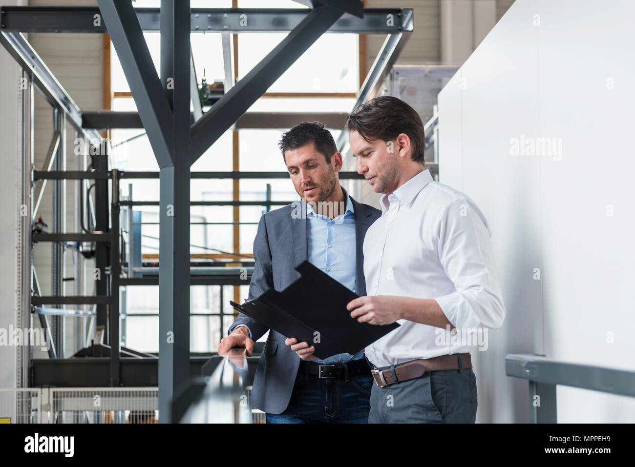 Two businessmen with clipboard talking in factory Stock Photo - Alamy