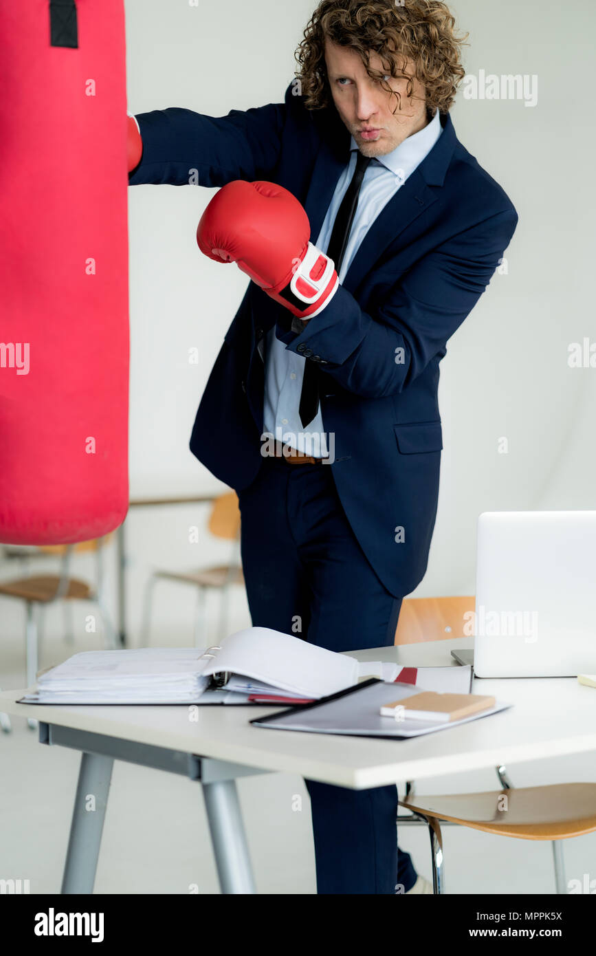 Stressed businessman hitting punch bag with boxing gloves in his office ...