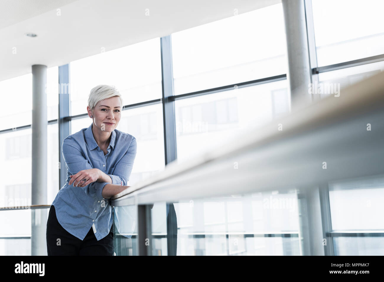 Portrait of woman in office building leaning on railing Stock Photo - Alamy