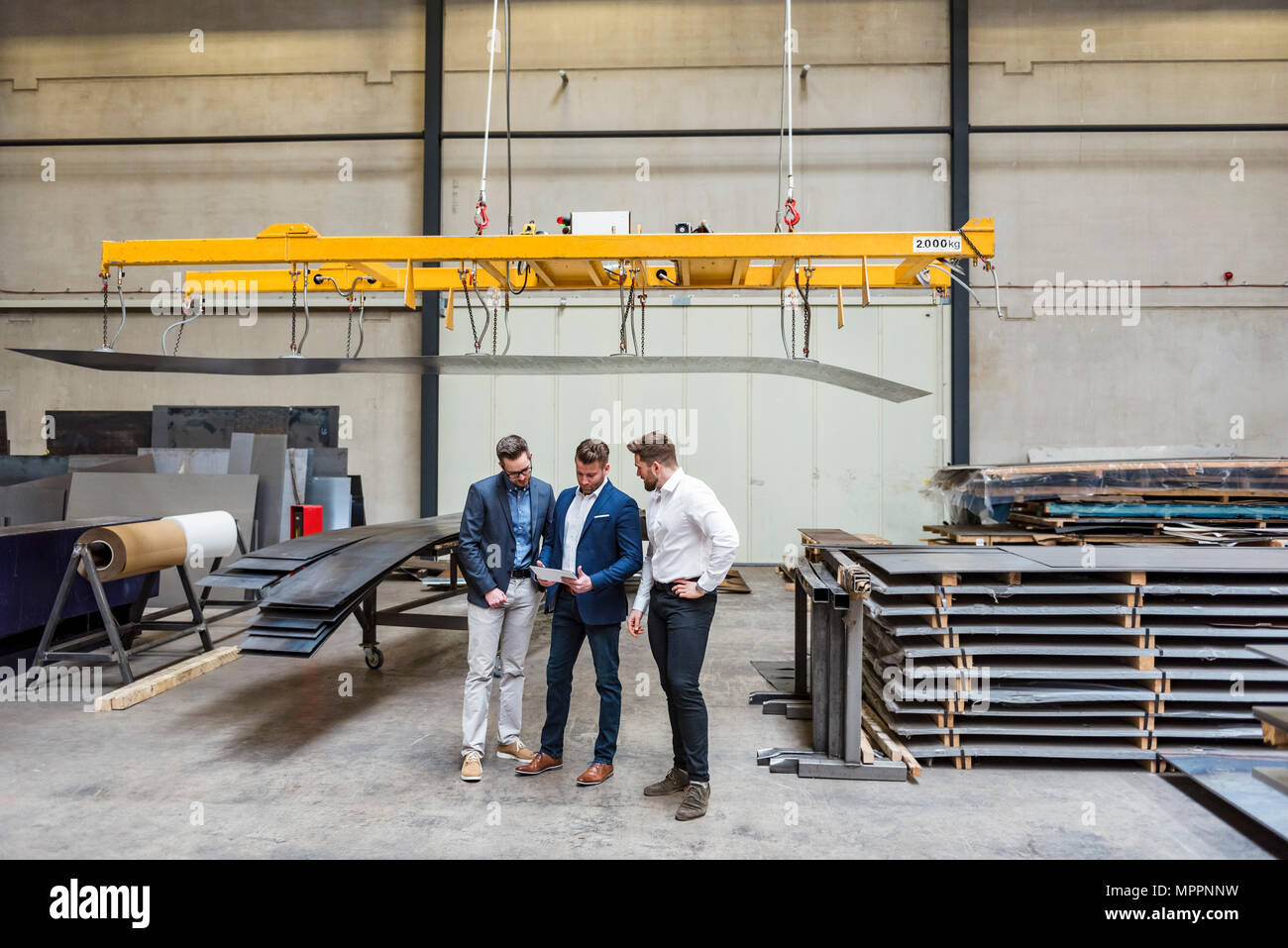 Three men standing on factory shop floor looking at tablet Stock Photo ...