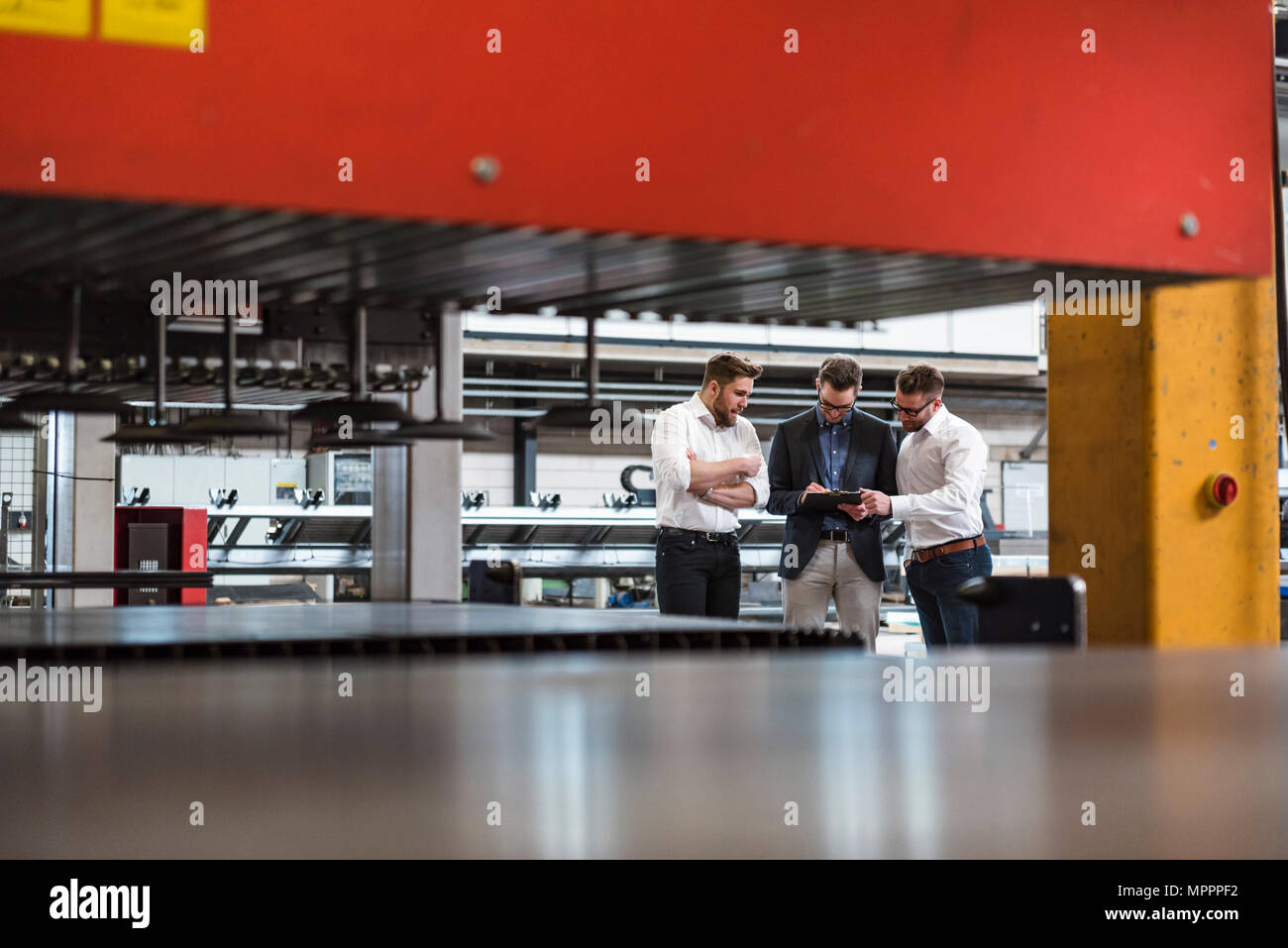 Three men sharing tablet on factory shop floor Stock Photo - Alamy