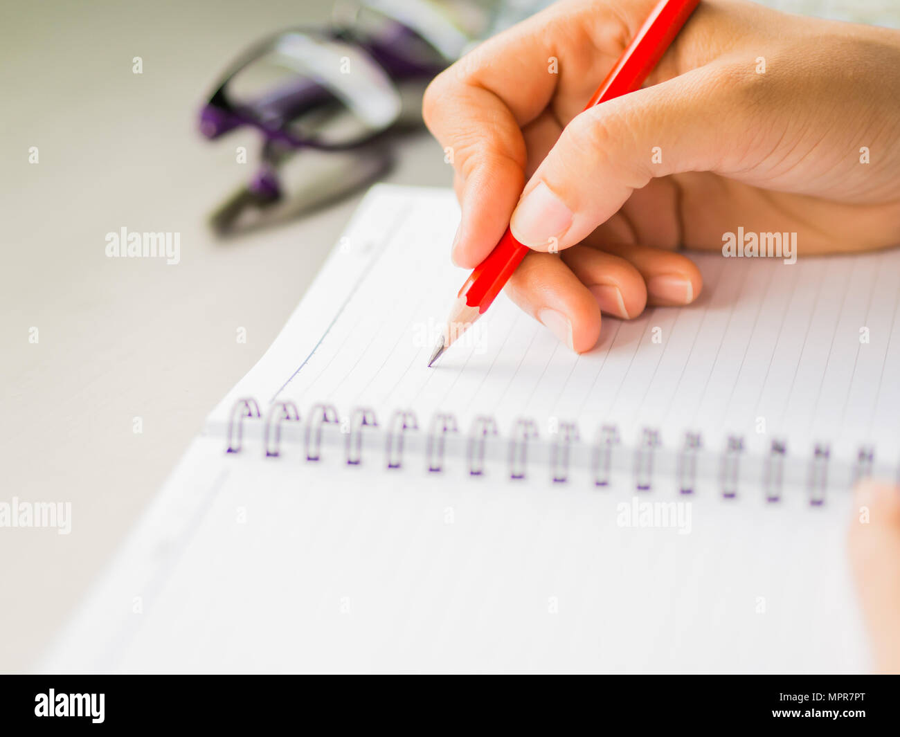 Closeup woman hand writing with red pencil and glasses background on ...