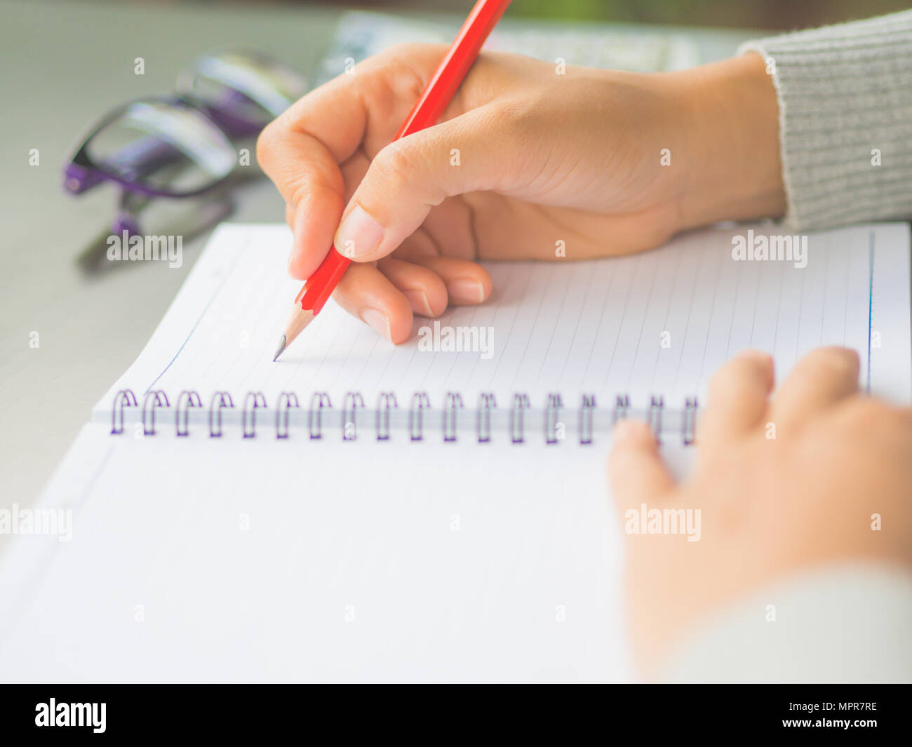 Closeup woman hand writing with red pencil and glasses background on ...