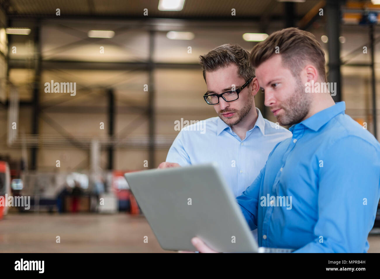 Two businessmen sharing laptop on factory shop floor Stock Photo - Alamy