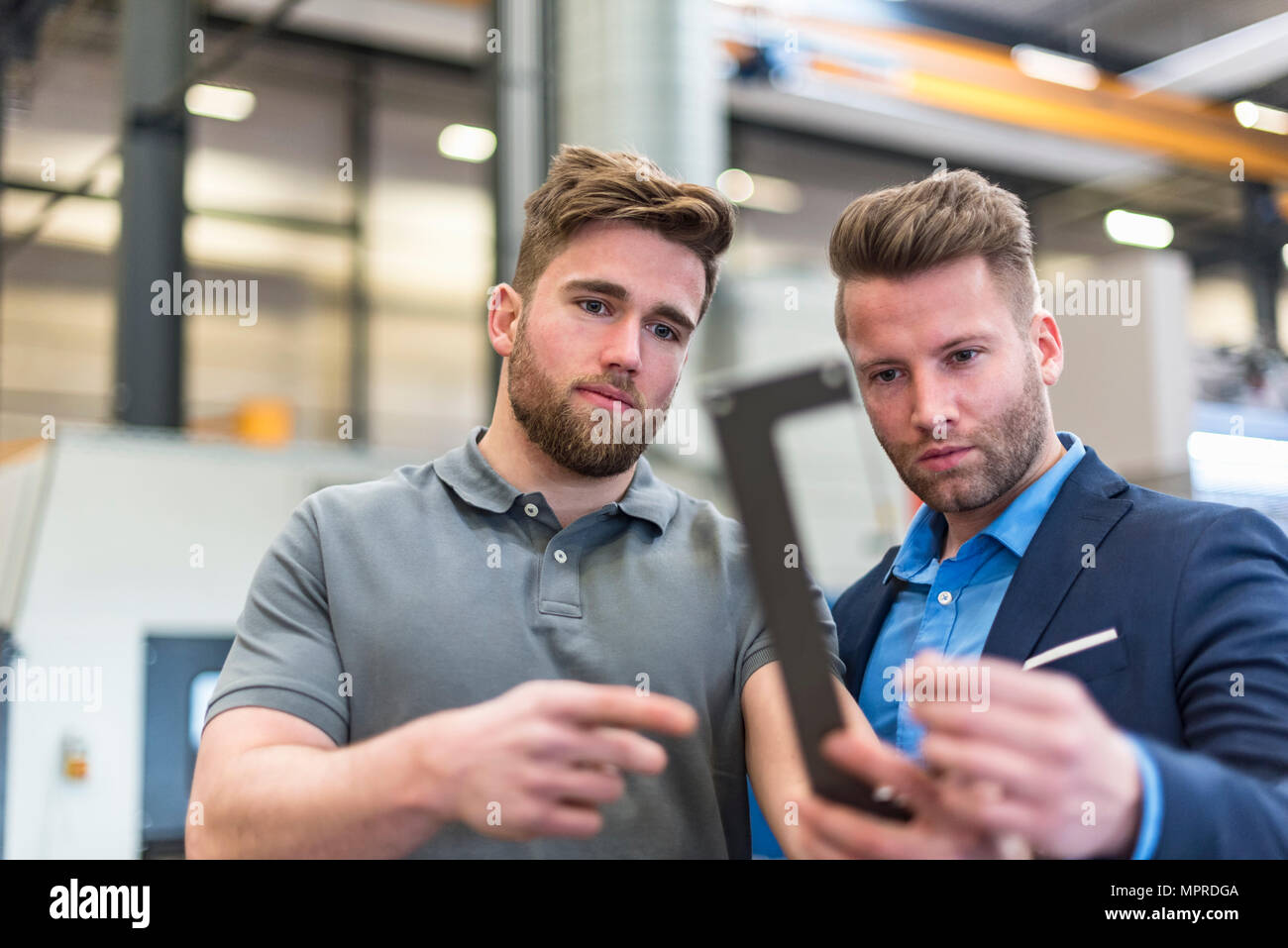 Employee and businessman examining workpiece on factory shop floor ...