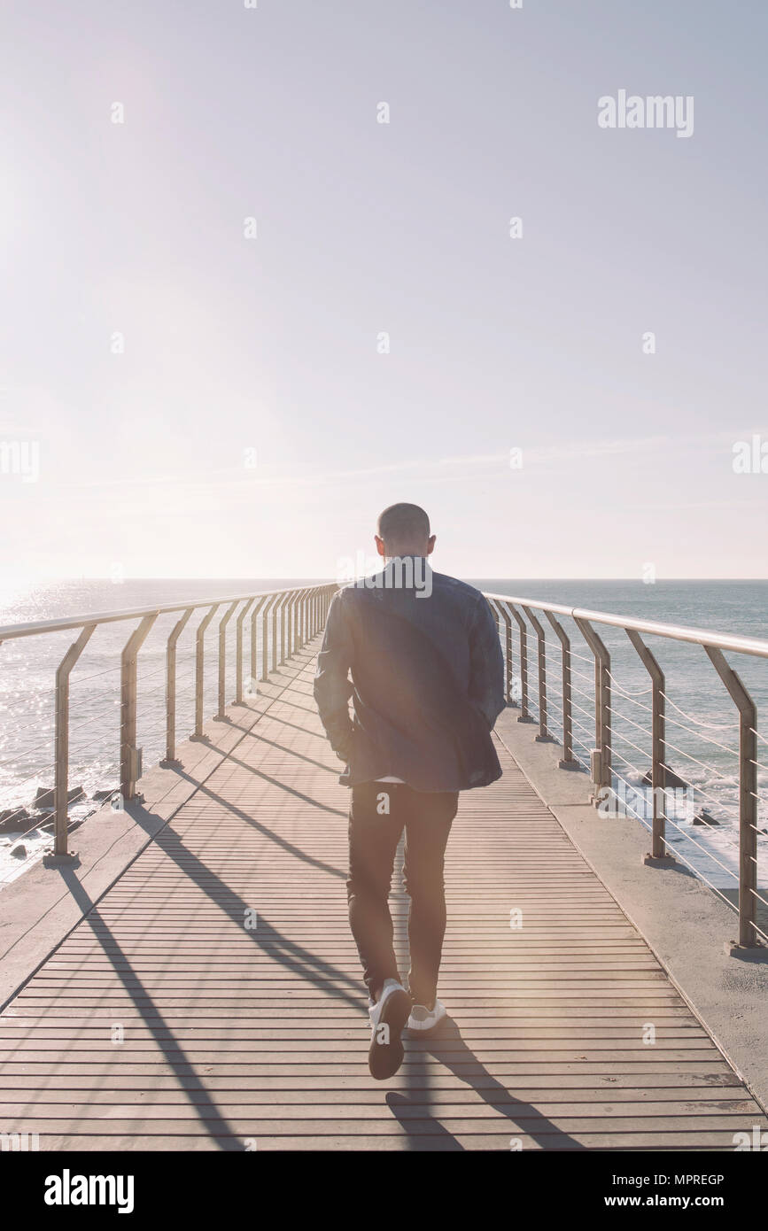 Back view of man walking on boardwalk at backlight Stock Photo - Alamy