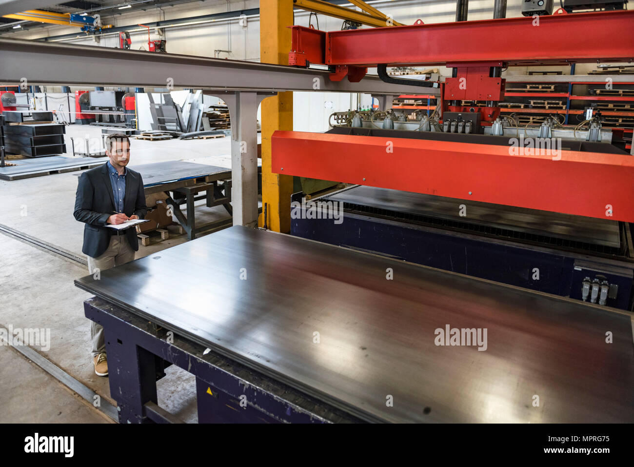 Businessman writing on clipboard on factory shop floor Stock Photo - Alamy