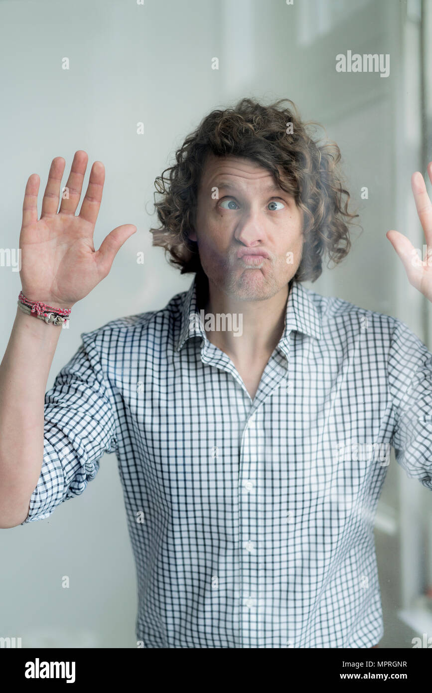Businessman pressing his face against glass pane, pulling faces Stock ...