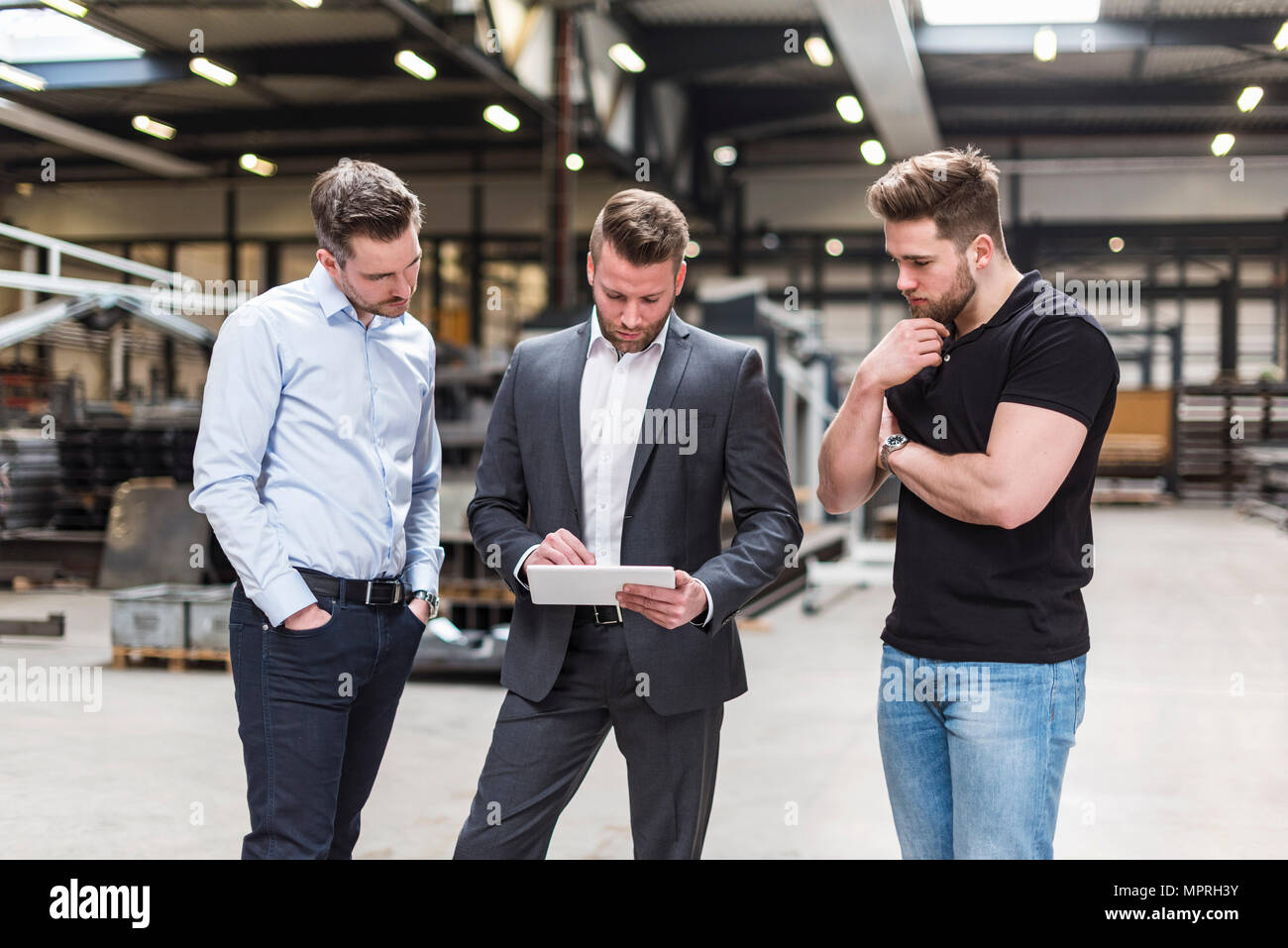 Three men sharing tablet on factory shop floor Stock Photo - Alamy