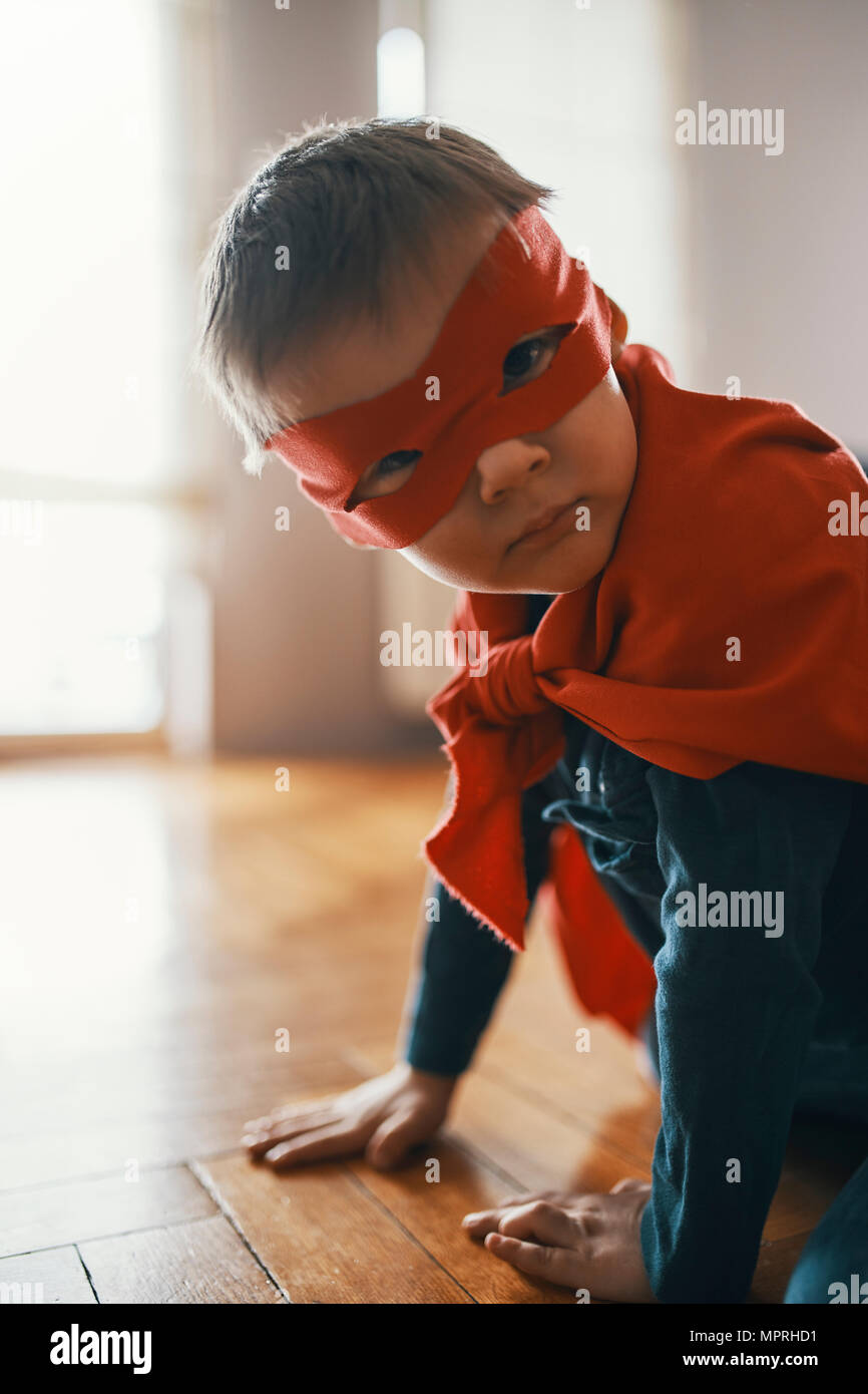 Little boy dressed up as a superhero crouching on the floor at home ...