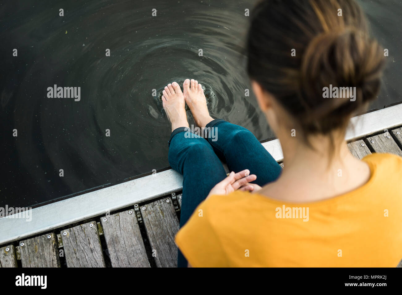 Woman sitting on jetty at a lake with feet in water Stock Photo - Alamy