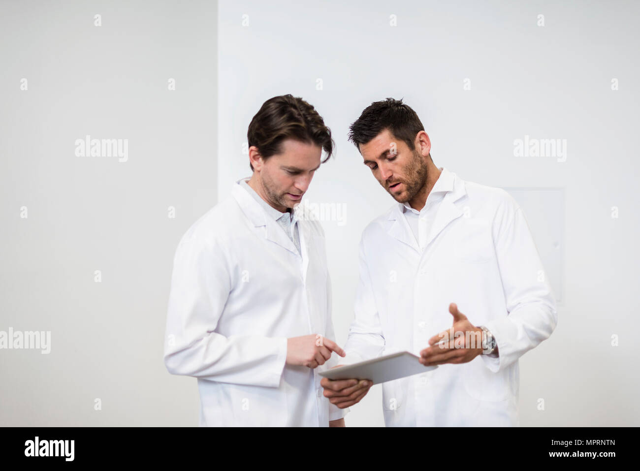 Two men wearing work coats sharing tablet Stock Photo - Alamy