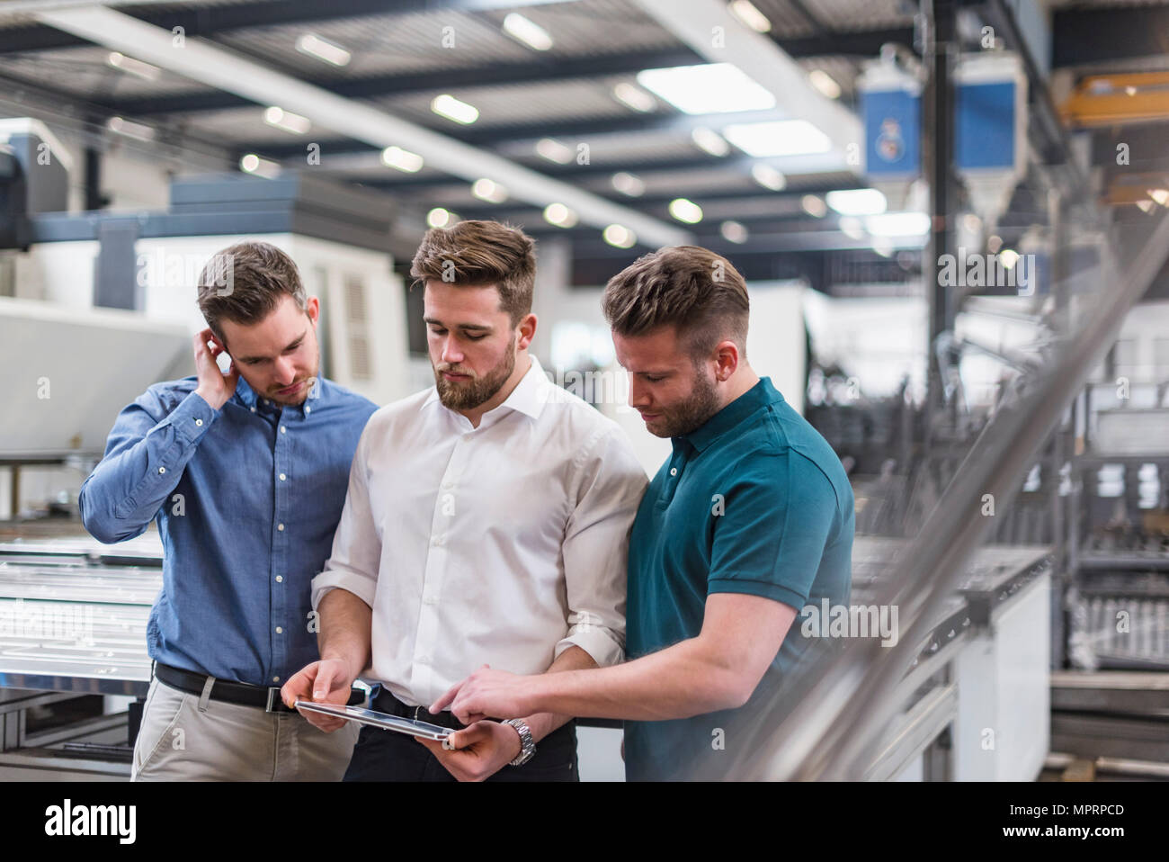 Three men sharing tablet on factory shop floor Stock Photo - Alamy