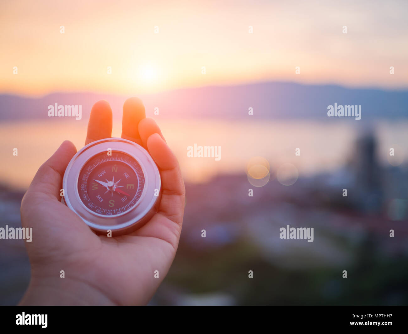 Closeup hand holding compass with mountain and sunset sky background ...