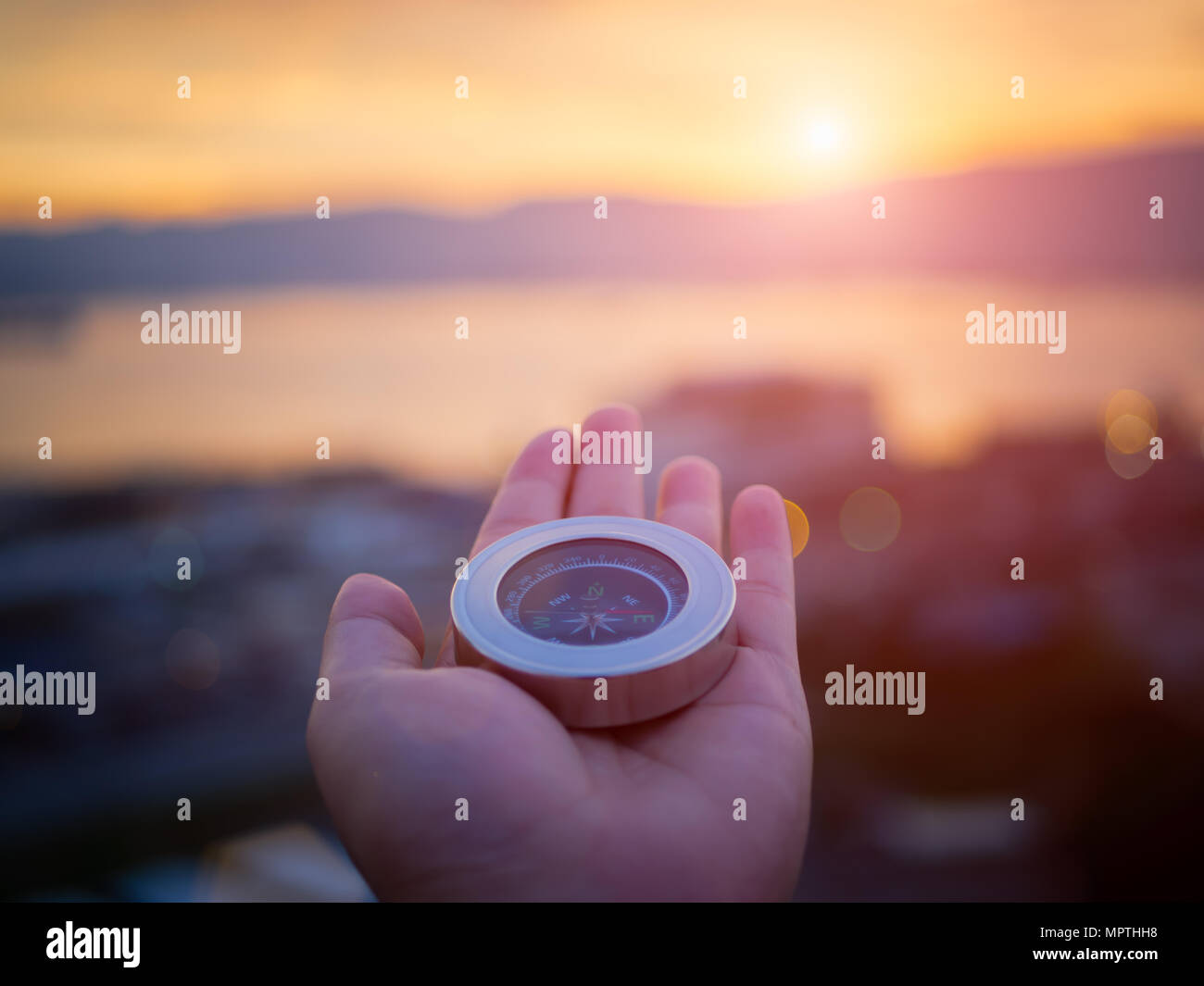 Closeup hand holding compass with mountain and sunset sky background ...