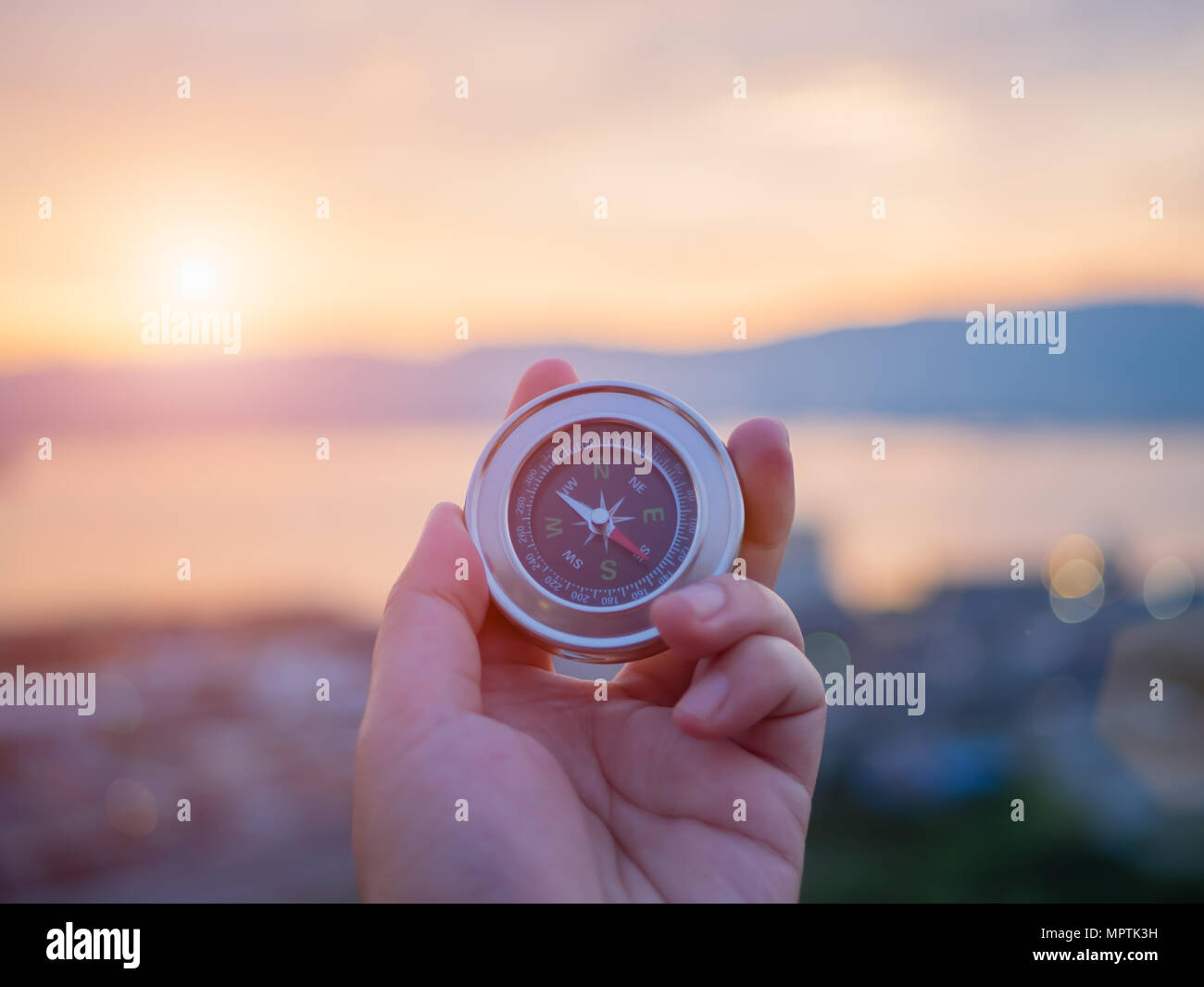 Closeup hand holding compass with mountain and sunset sky background ...