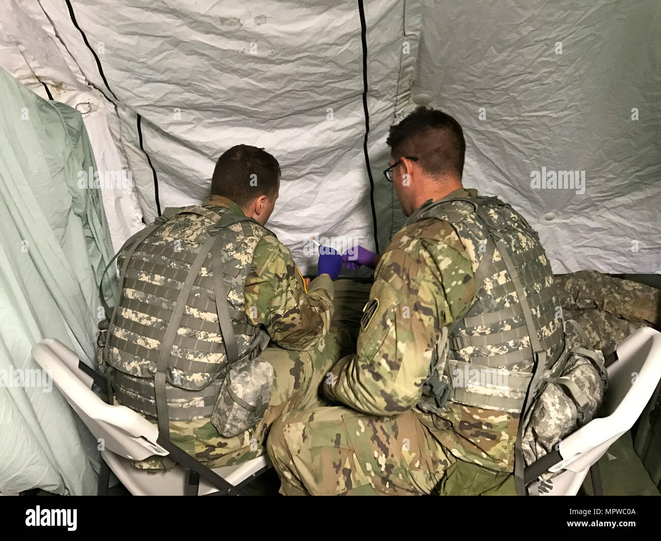 Two Soldiers administer medical assistance to a Soldier with an eye ...