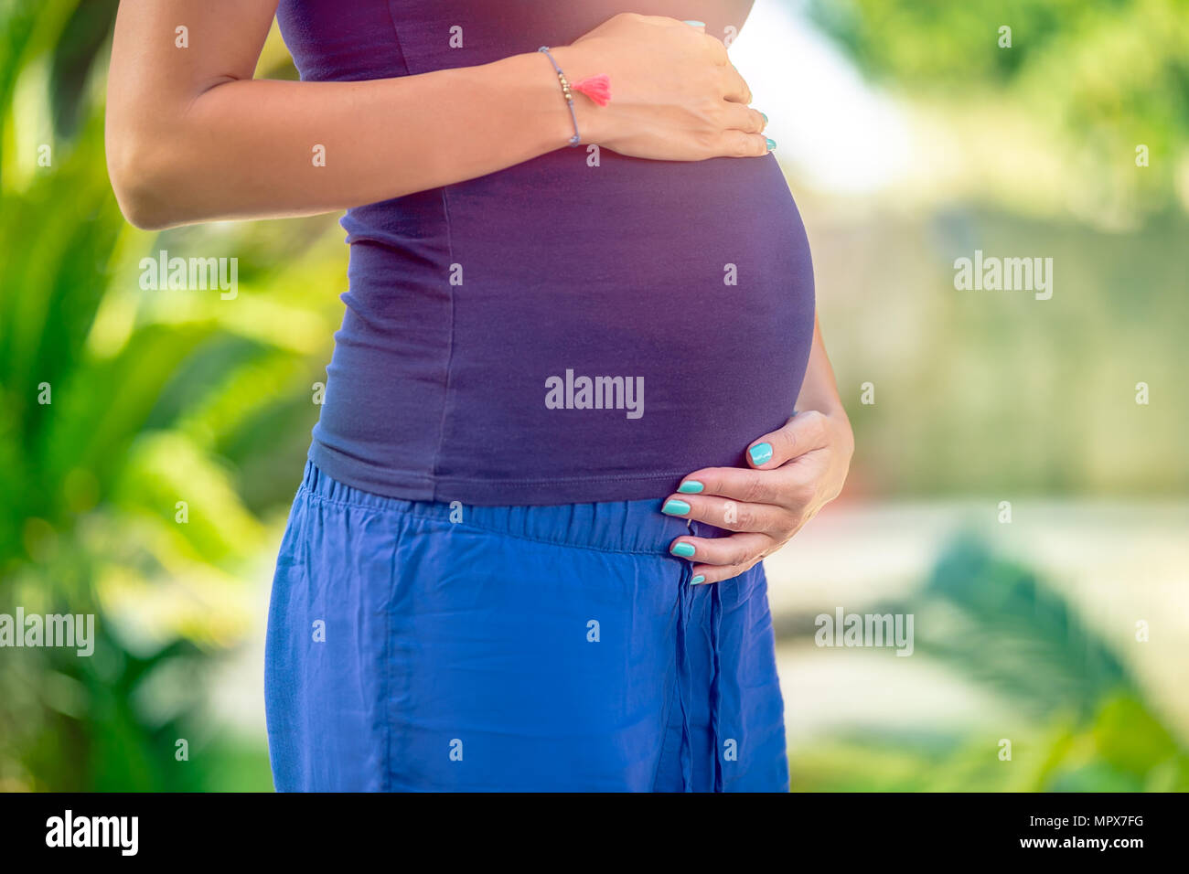 Closeup photo of a tummy of pregnant woman standing in the park, with ...