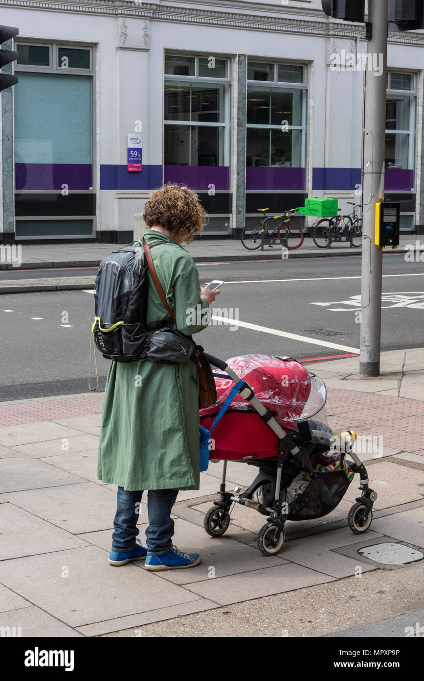 a woman pushing a pushchair with a child whilst using a mobile phone at ...