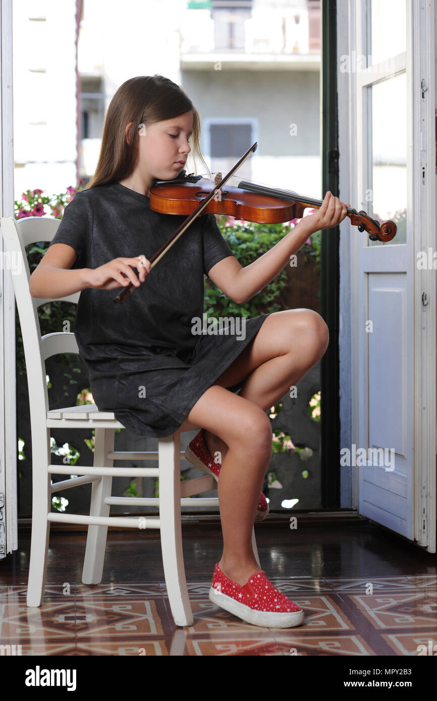 Girl playing violin while siting on chair at home Stock Photo - Alamy