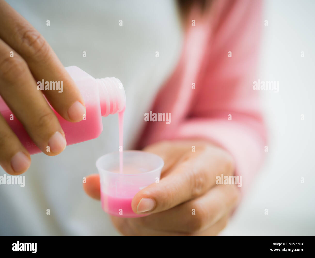 Closeup woman pouring medication or antipyretic syrup from bottle to ...