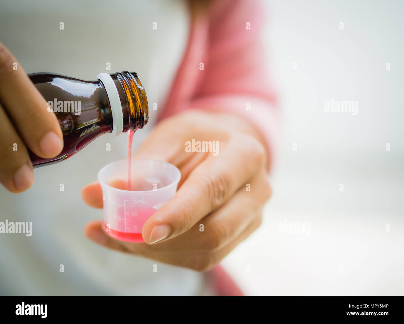 Closeup woman pouring medication or antipyretic syrup from bottle to ...