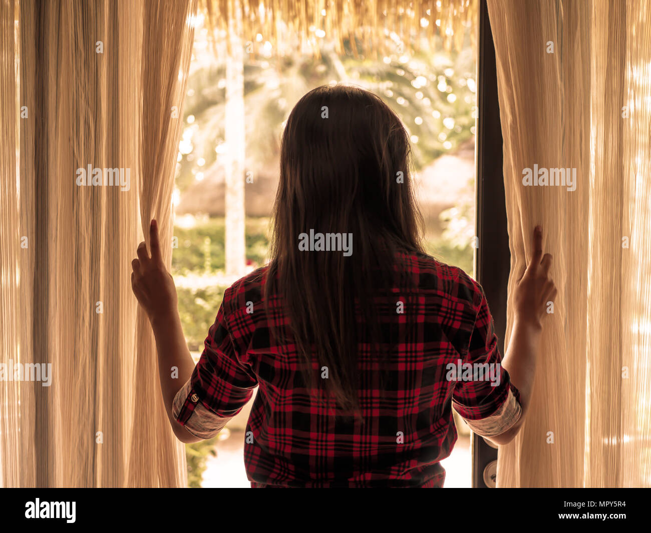 Retro woman holding the curtains open to look out of a large light ...