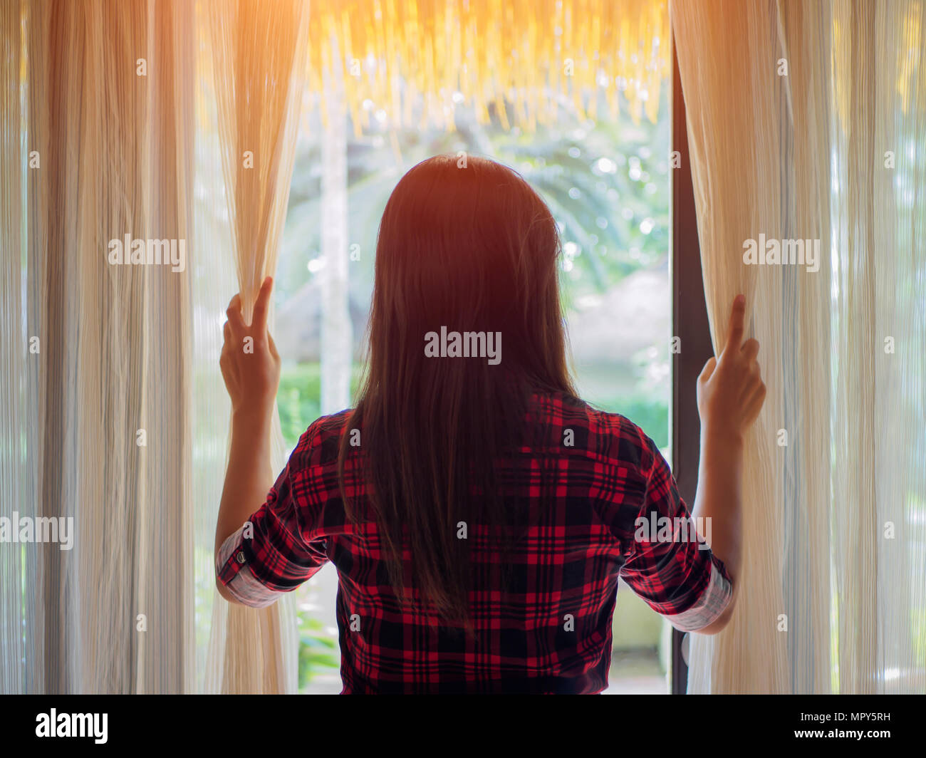 Young woman holding the curtains open to look out of a large light ...