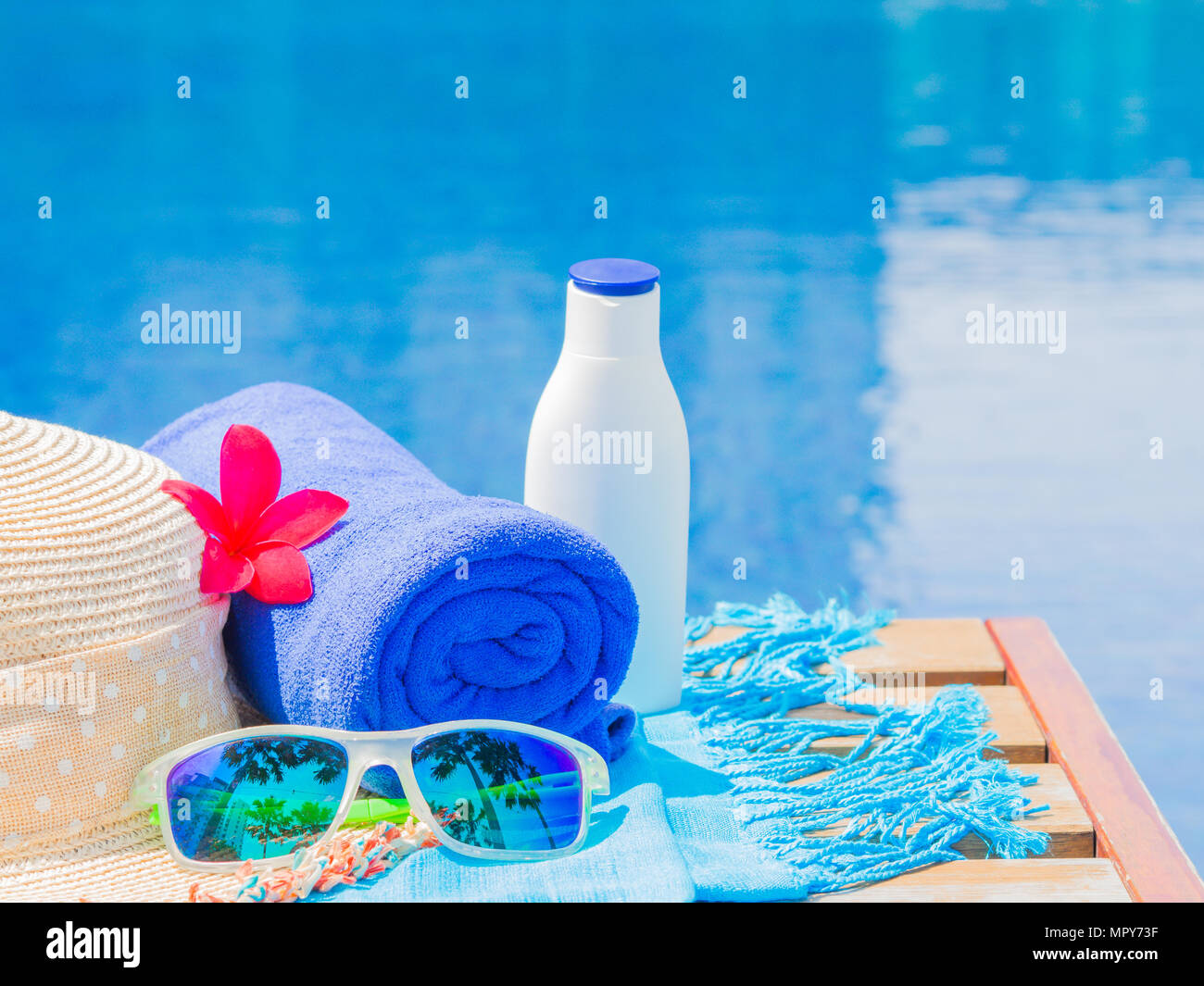 Sunglasses, beach hat, blue towel and sunscreen at the side of swimming ...
