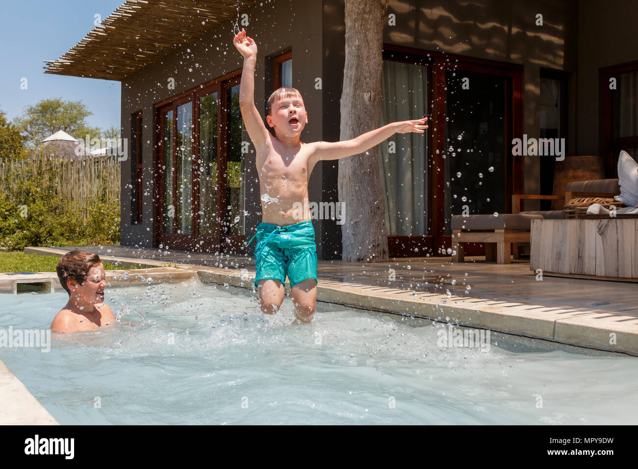 Shirtless playful boy jumping while brother swimming in plunge pool ...