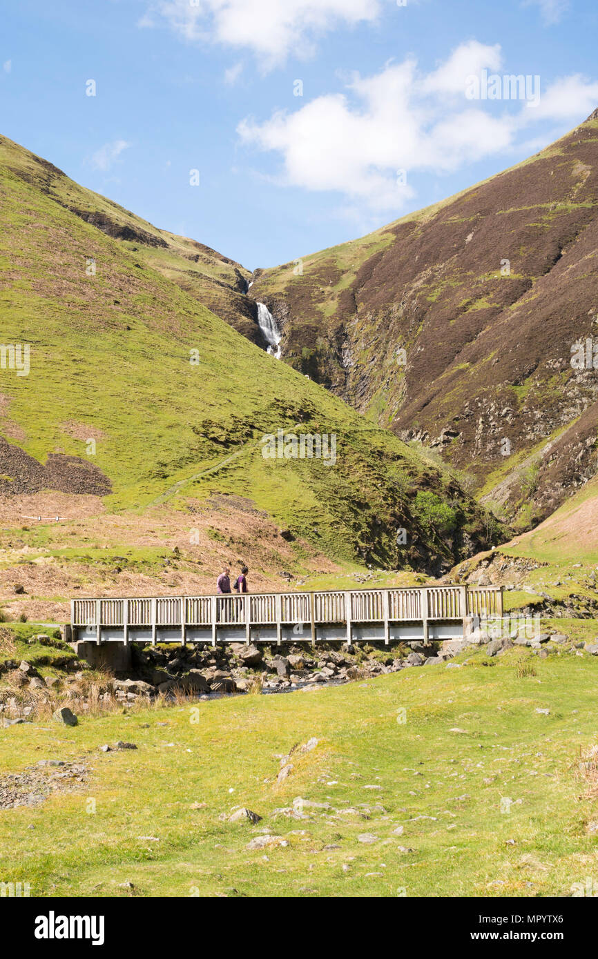 Two walkers cross the footbridge over the Tail Burn beneath The Grey ...