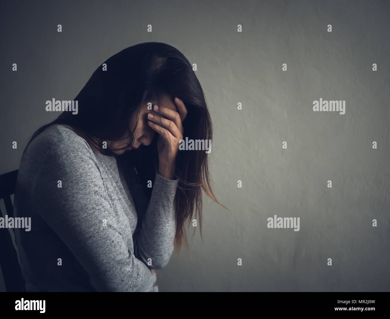 Depressed woman sitting on a chair in dark room at home. Lonly , sad ...
