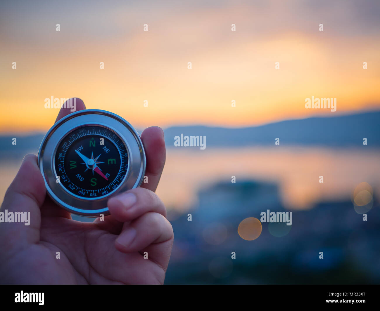 Closeup hand holding compass with mountain and sunset sky background ...