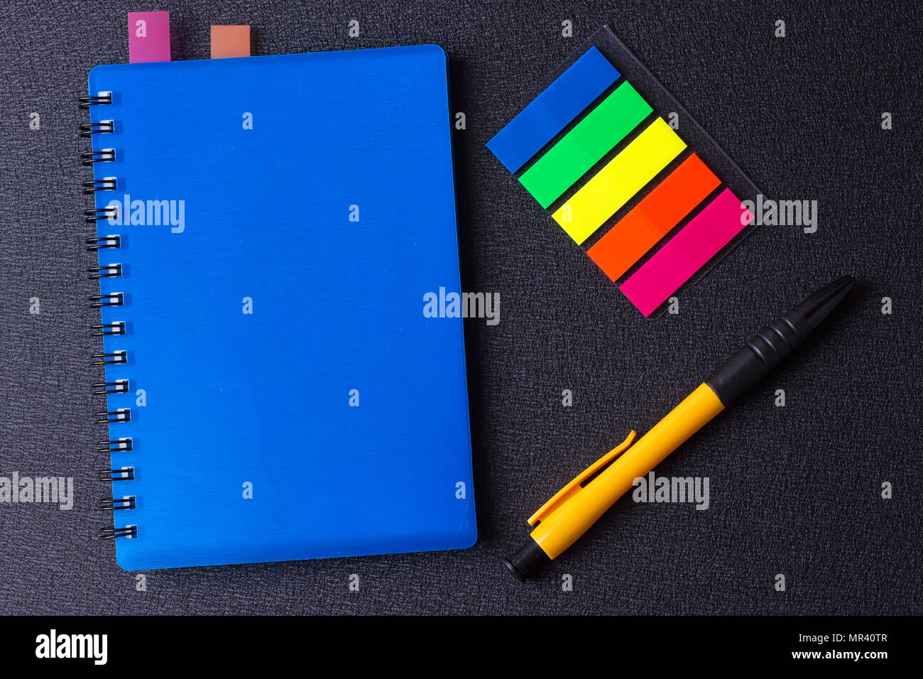 Blue notepad with multi-colored stickers and pen on a black background ...