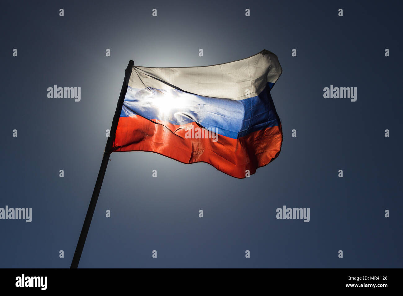 russian tricolor flag flying in slow motion and back lit by the sun ...