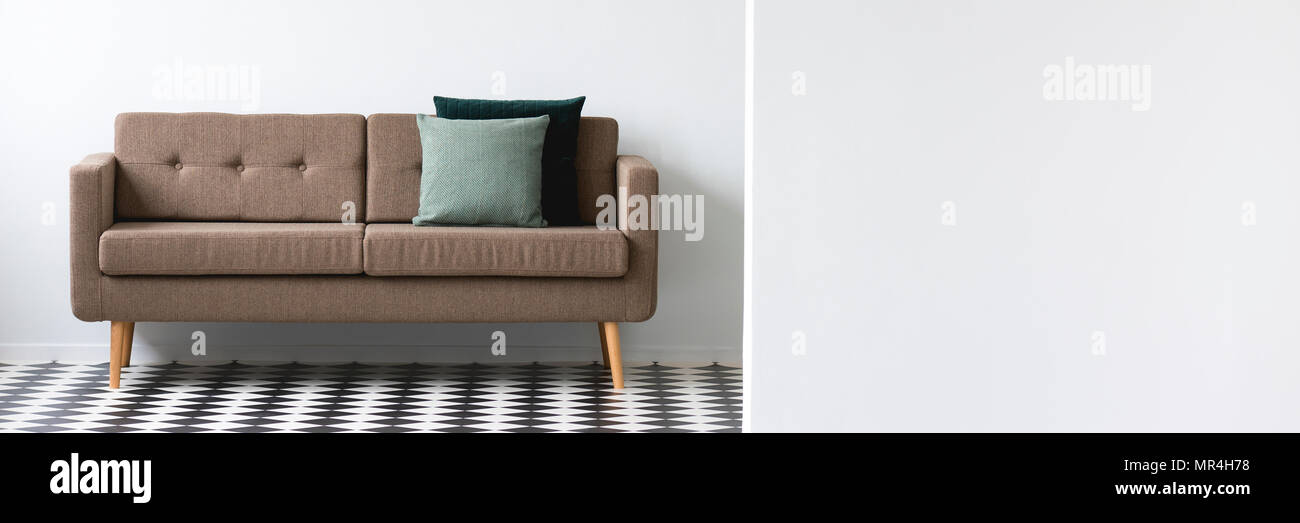 Brown couch with two green cushions standing in open space white ...